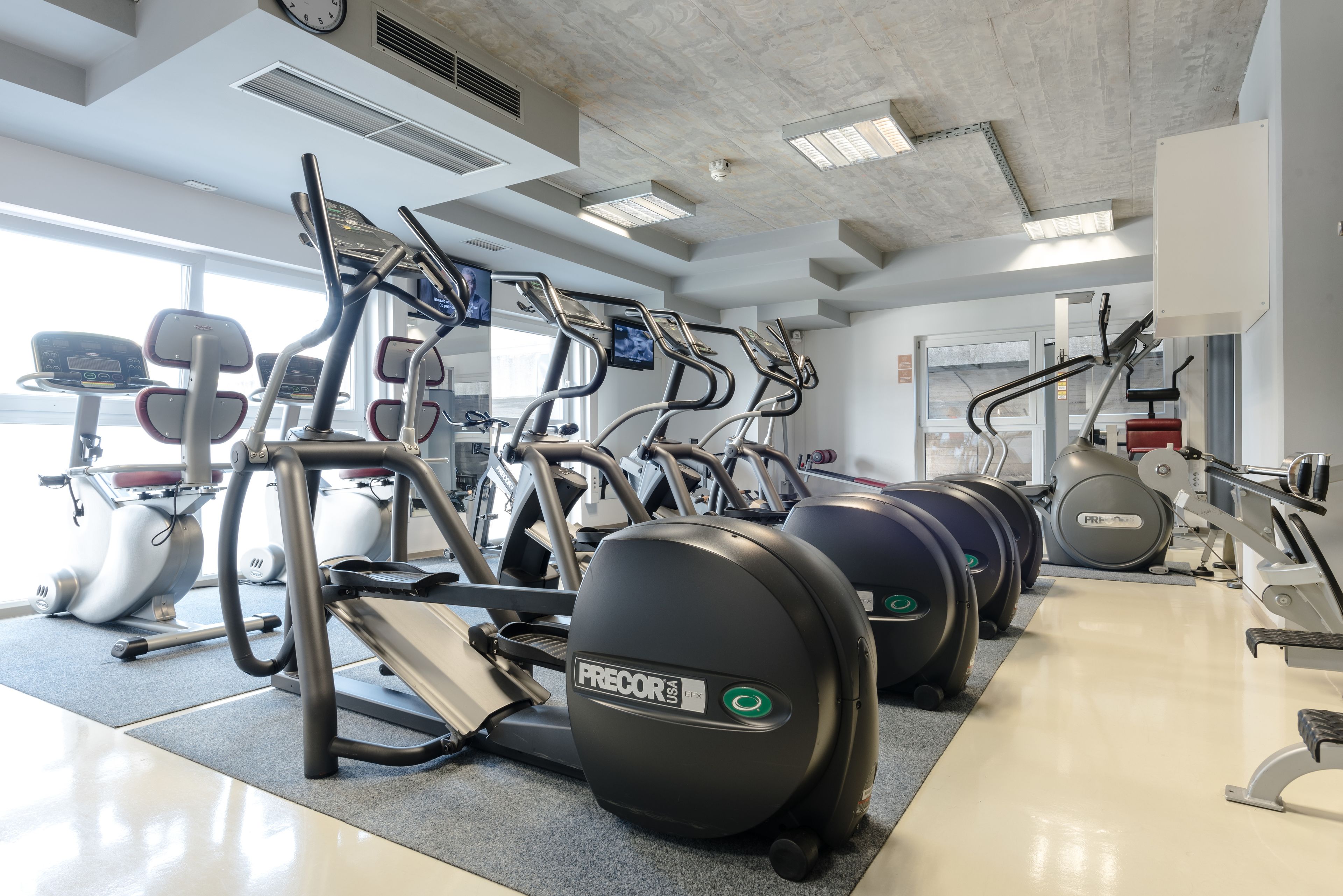 Uma academia com vários equipamentos de exercícios, incluindo esteiras e elípticos, dispostos em fileiras.