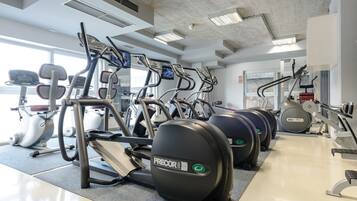 Uma academia com vários equipamentos de exercícios, incluindo esteiras e elípticos, dispostos em fileiras.