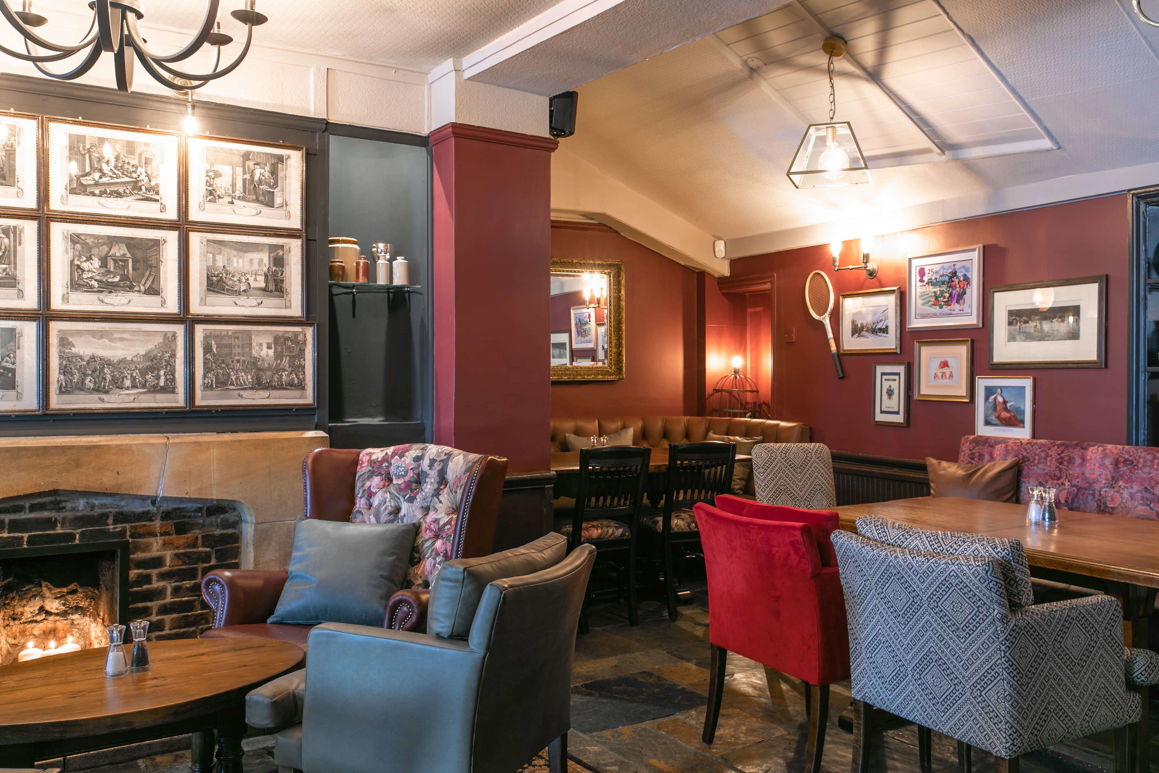 Um restaurante acolhedor com lareira, vários espaços para sentar e uma parede decorada com quadros.
