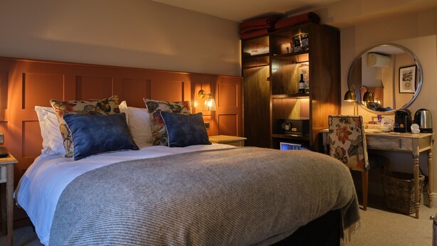 Quarto de hotel com uma cama grande, um guarda-roupa de madeira, uma escrivaninha com cadeira e um espelho redondo na parede.