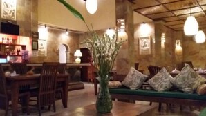 Interior de restaurante com mobiliário de madeira, um vaso verde com flores e luminárias pendentes.