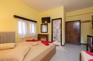 Quarto de hotel com uma cama, um guarda-roupa de madeira, casa de banho com chuveiro e uma televisão fixada na parede.