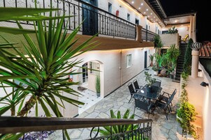 Um pátio com área de refeições, plantas em vasos e uma escadaria que leva a um andar superior.