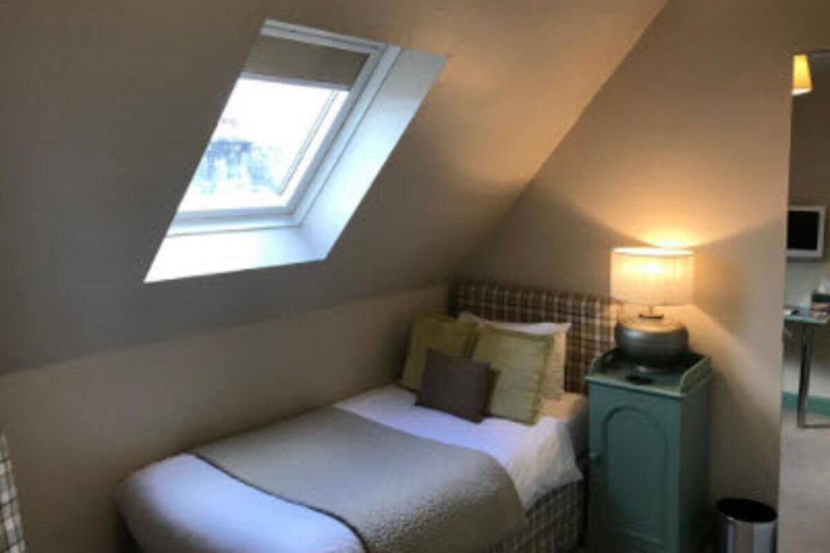 Um quarto pequeno e acolhedor com uma cama de solteiro, uma janela e uma mesa de cabeceira.