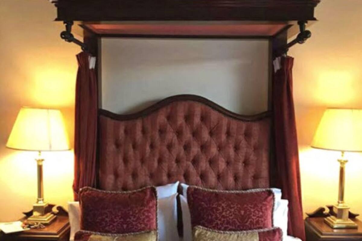 Cama com cabeceira estofada, duas luminárias de apoio e dois travesseiros decorativos.