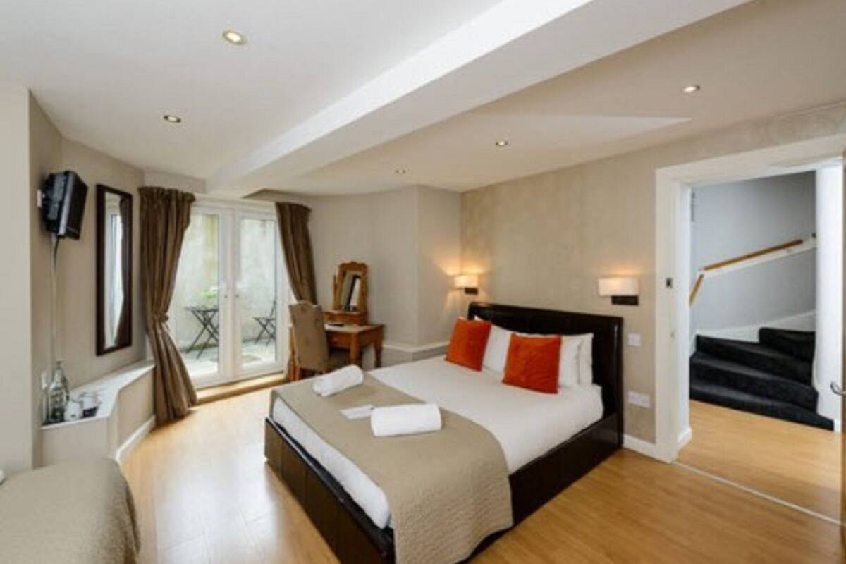 Quarto de hotel com uma cama grande, uma escrivaninha com cadeira, televisão fixada na parede e escada para um andar superior.