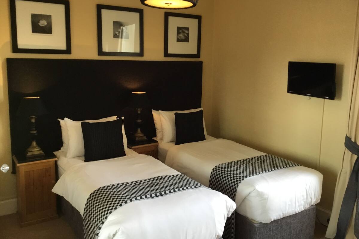 Quarto de hotel com duas camas, uma televisão presa à parede e quadros emoldurados acima das camas.