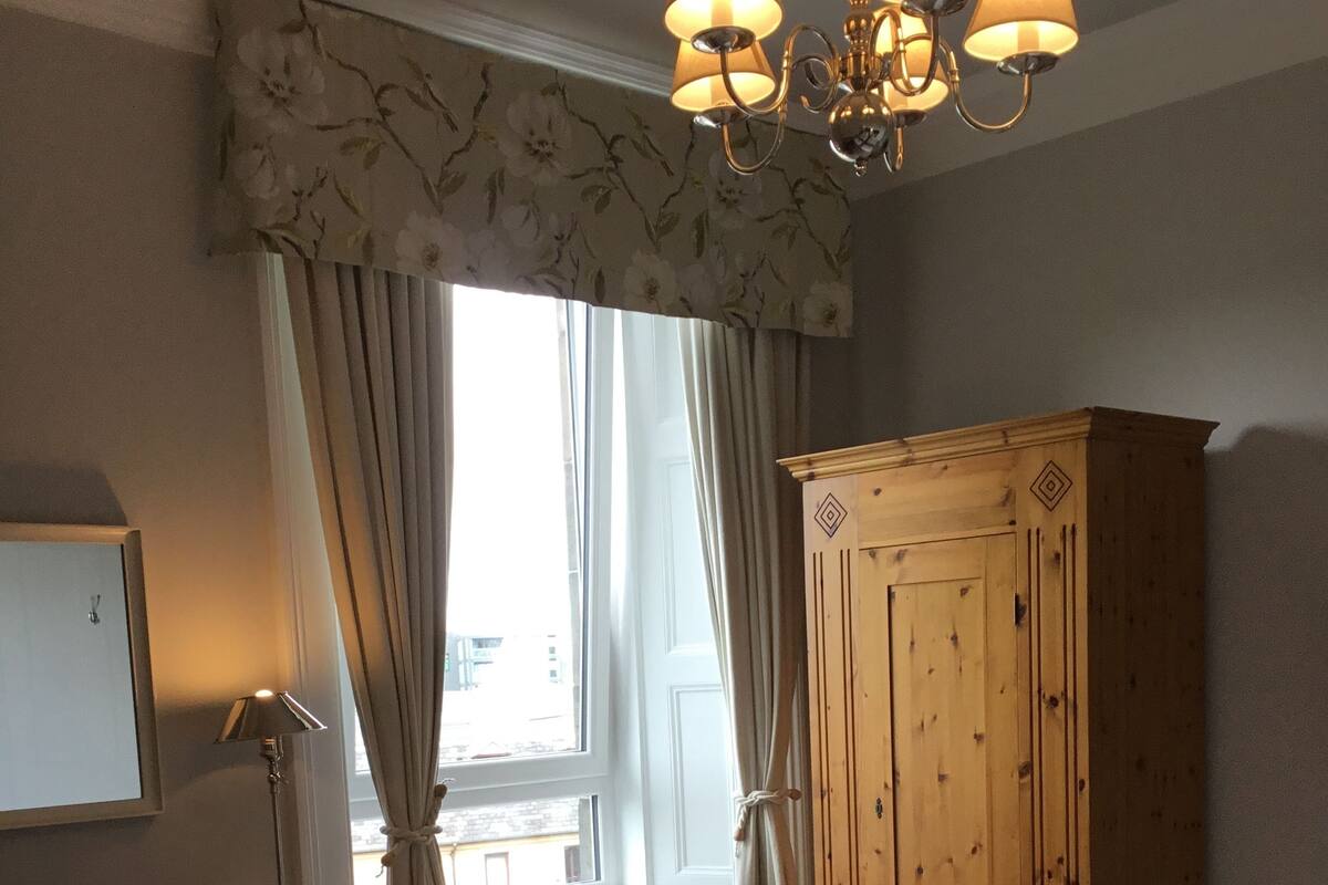 Quarto de hotel com guarda-roupa de madeira, uma secretária com abajur, duas camas e uma janela com cortinas.