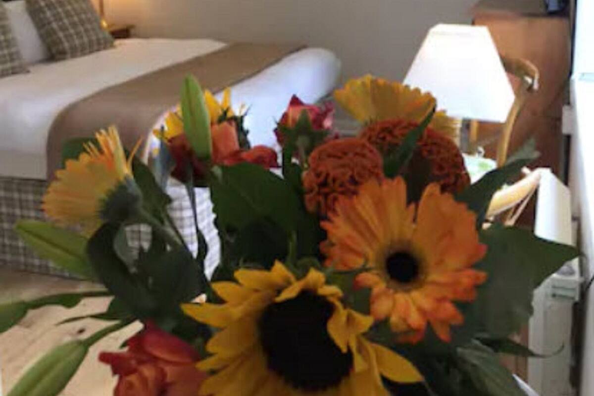 Quarto de hotel com uma cama, mesa de cabeceira, abajur e um vaso de flores.