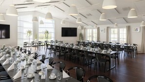 Sala de conferência com várias mesas preparadas para uma reunião, equipada com cadeiras, mesas e uma tela grande.