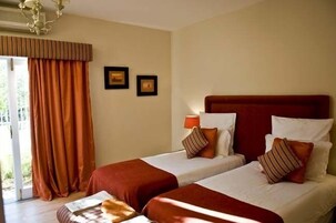 Quarto de hotel com duas camas, um candelabro e vista para o exterior.