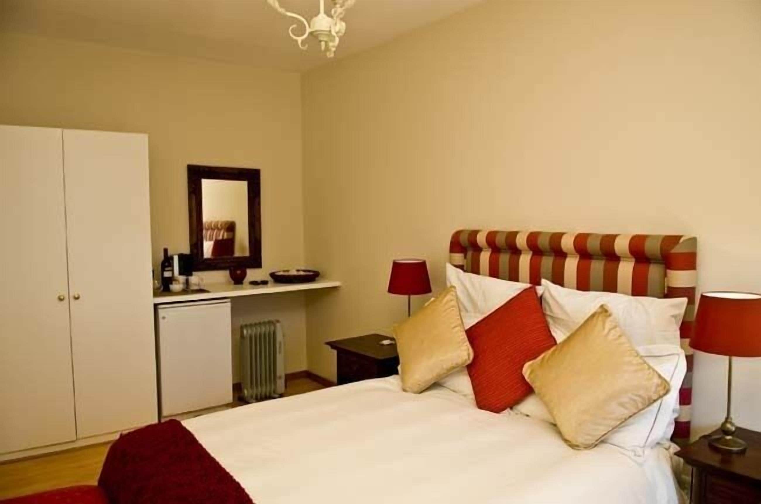 Quarto de hotel com cama, mesas de cabeceira, guarda-roupa, espelho e radiador.