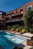 Um edifício moderno com piscina, espreguiçadeiras de madeira e um céu azul límpido.
