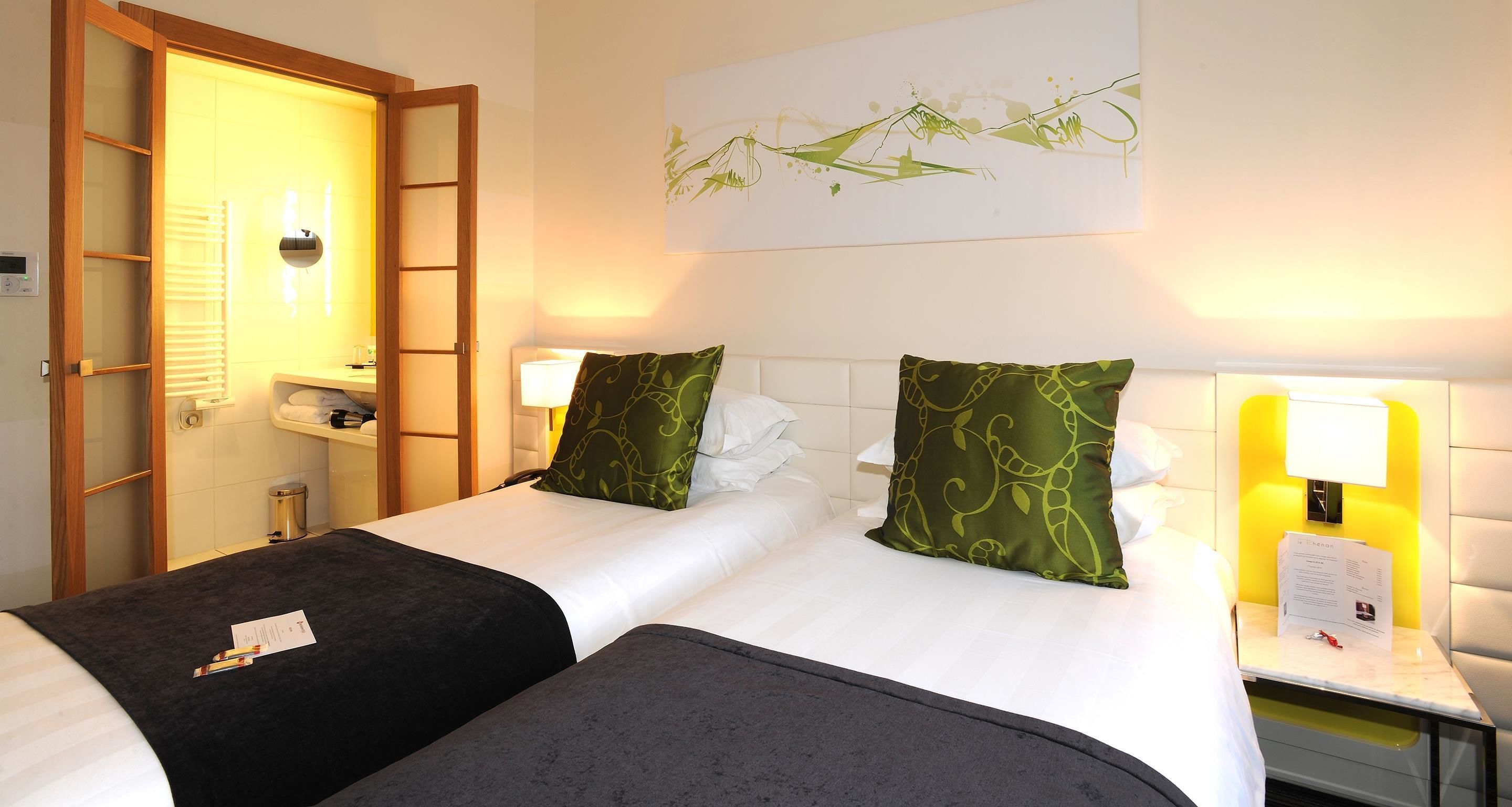 Quarto de hotel com duas camas, banheiro e mesa de cabeceira com abajur.