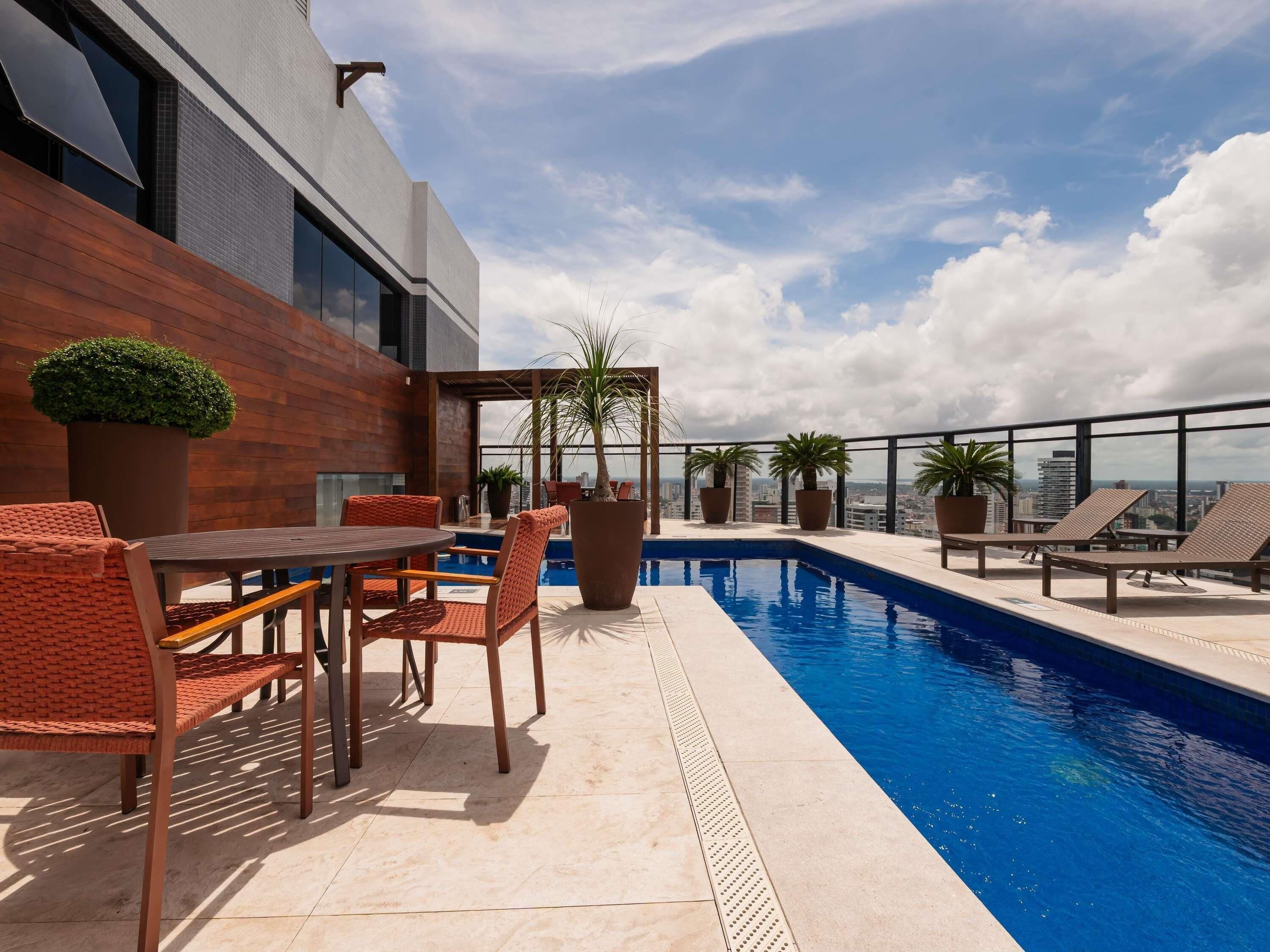 Uma área de piscina no terraço com espreguiçadeiras, uma mesa e plantas em vasos.