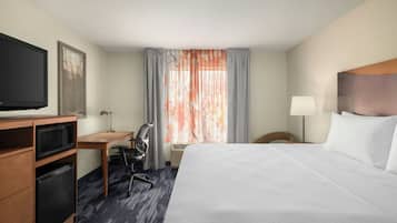Quarto de hotel com cama, escrivaninha, televisão e janela com cortinas.