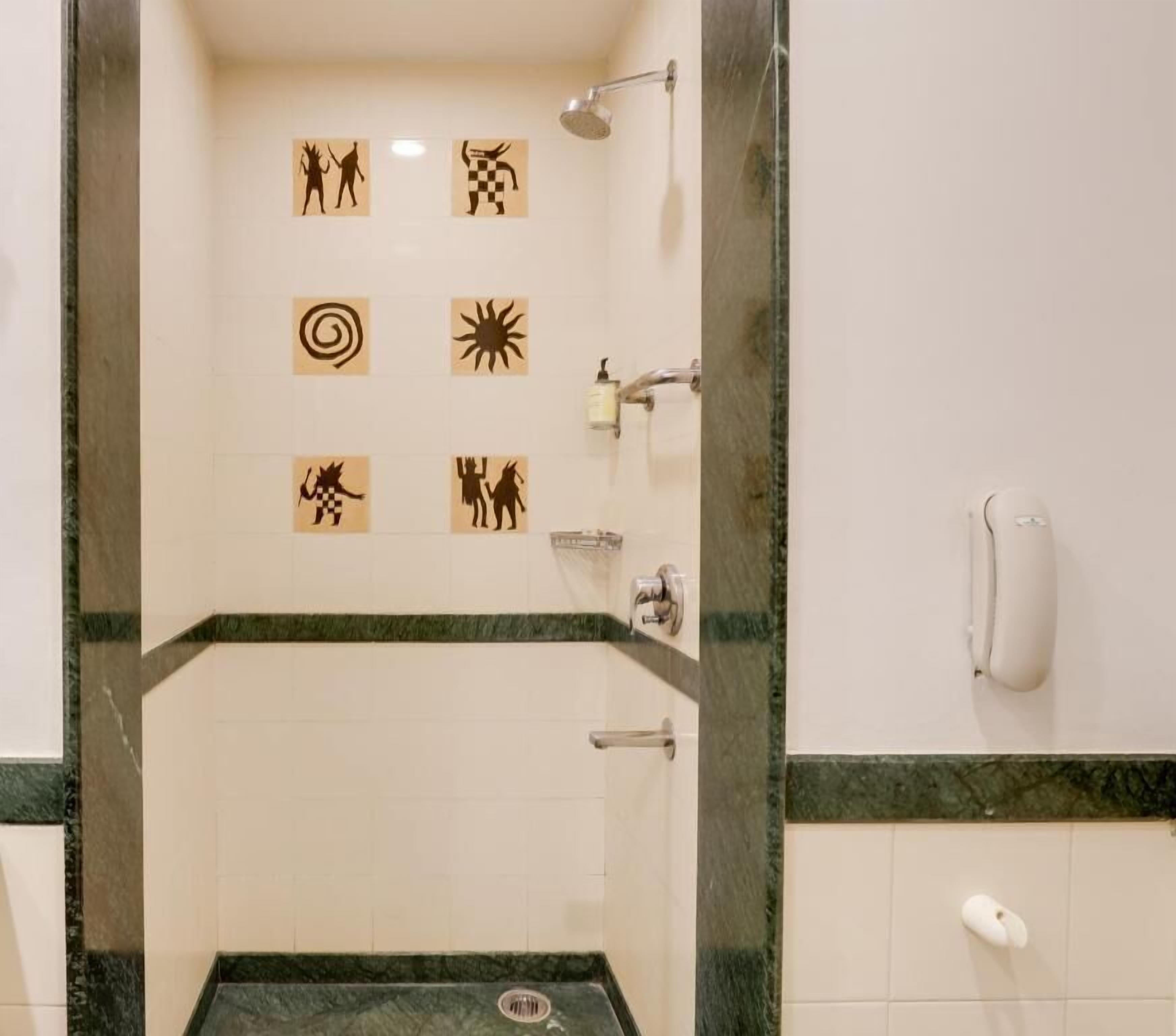 Casa de banho com chuveiro, sanita e lavatório. Apresenta dispensadores de sabonete na parede e um secador de mãos.