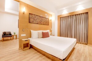 Quarto de hotel moderno com uma cama grande, cabeceira de madeira, uma obra de arte na parede, mesa de cabeceira e uma janela com cortinas.