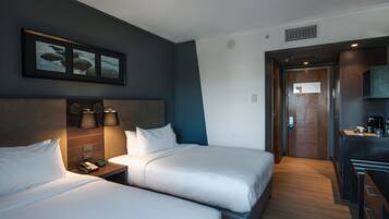 Quarto de hotel com duas camas, uma cozinha compacta e um quadro na parede.