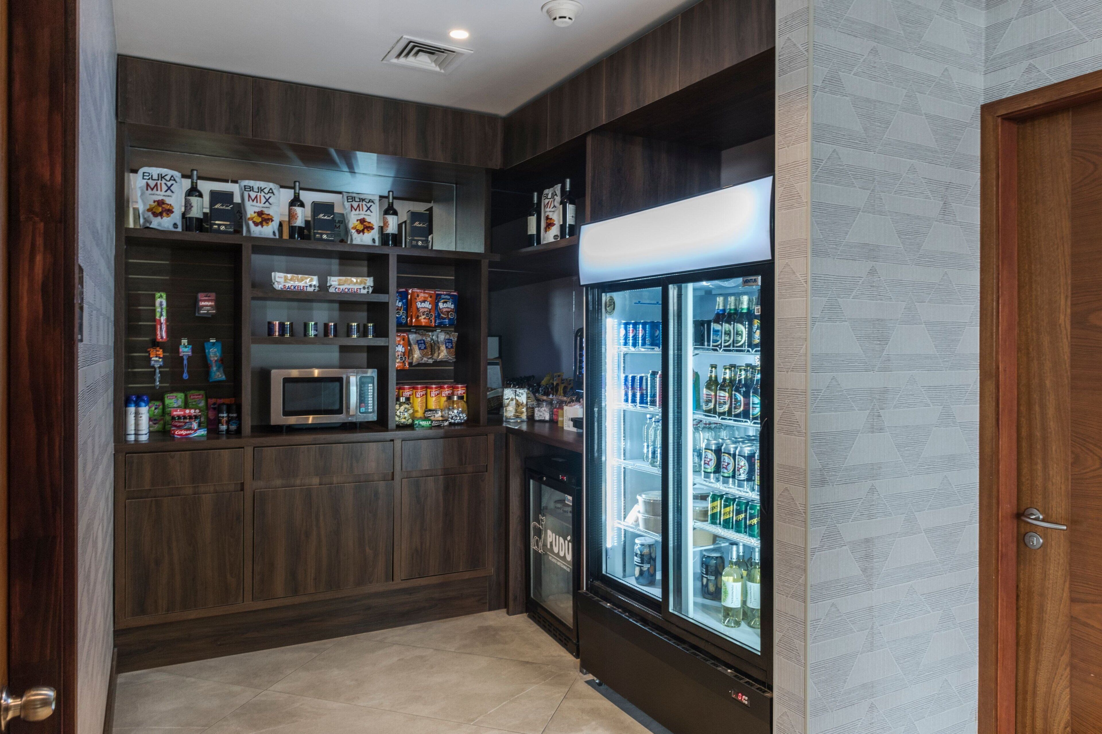 Uma cozinha moderna com micro-ondas embutido, geladeira abastecida com bebidas e prateleiras com lanches e temperos.