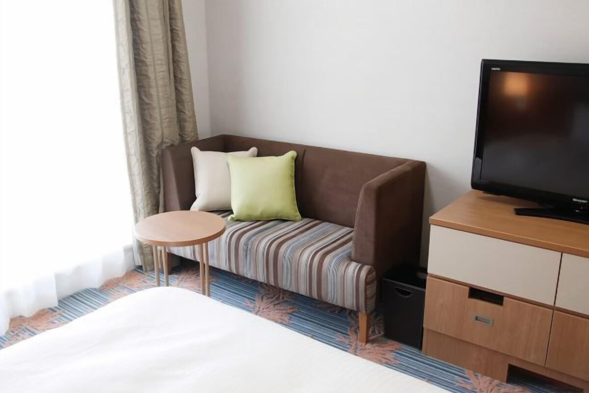 Quarto de hotel com sofá, televisão, mesa redonda pequena e cama.