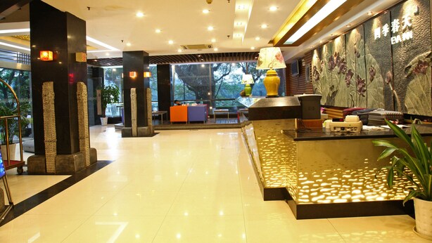 Um hall de hotel moderno com balcão de recepção, área de estar e uma grande janela com vista para árvores.