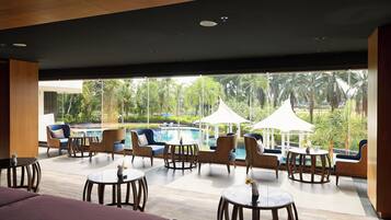 Uma área de estar moderna com mobiliário de madeira, piscina e vista para palmeiras.