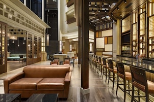 Um hall amplo com sofá de couro, área de bar com bancos e espaço para sentar com mesas e cadeiras.