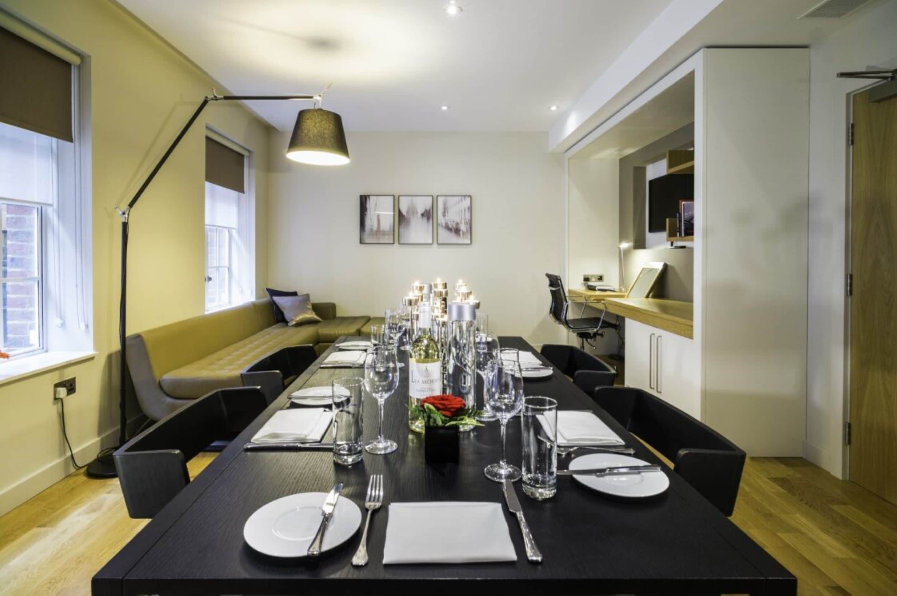 Uma área de refeições com uma mesa comprida posta para uma refeição, um sofá e uma luminária.