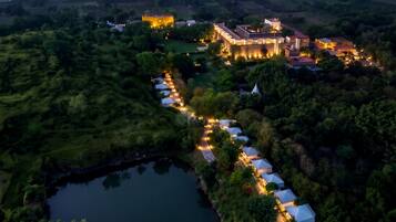 Vista aérea de um resort com um lago, edifícios interligados e um caminho bem iluminado.