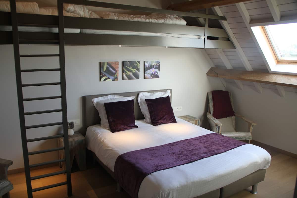 Um quarto com cama de solteiro, uma cama individual com cobertor roxo, escada de madeira, uma cadeira e um claraboia.