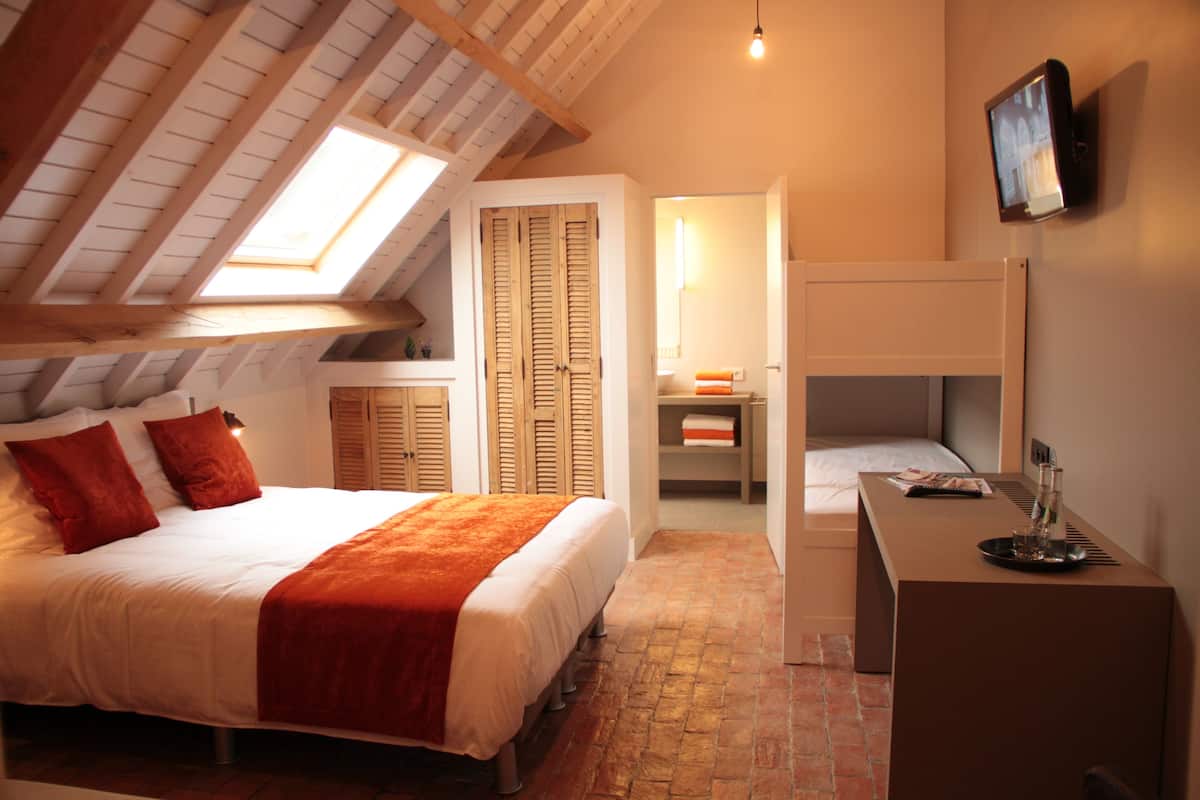 Quarto com uma cama grande, uma escrivaninha e uma televisão na parede.