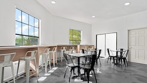 Um quarto amplo com teto alto, grandes janelas e uma mistura de cadeiras brancas e pretas ao redor de uma mesa central.