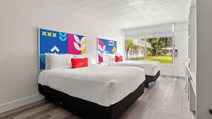 Quarto de hotel com duas camas, roupa de cama branca, almofadas vermelhas e arte abstrata colorida nas paredes.