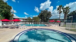 Uma área de piscina com várias piscinas, espreguiçadeiras e guarda-sóis vermelhos.