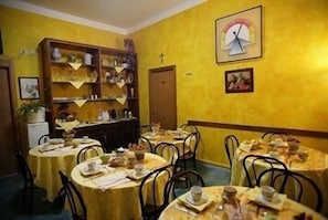 Uma área de refeições com mesas redondas, cadeiras e um buffet com diversos pratos.