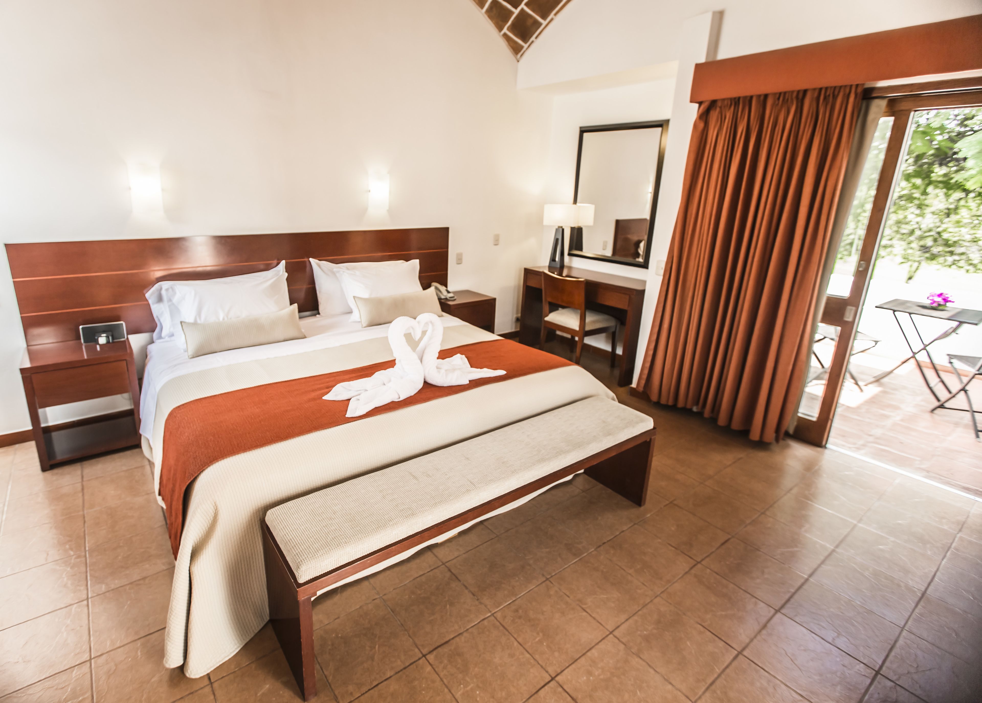 Quarto de hotel com uma cama grande, uma escrivaninha, uma cadeira e vista para o exterior.