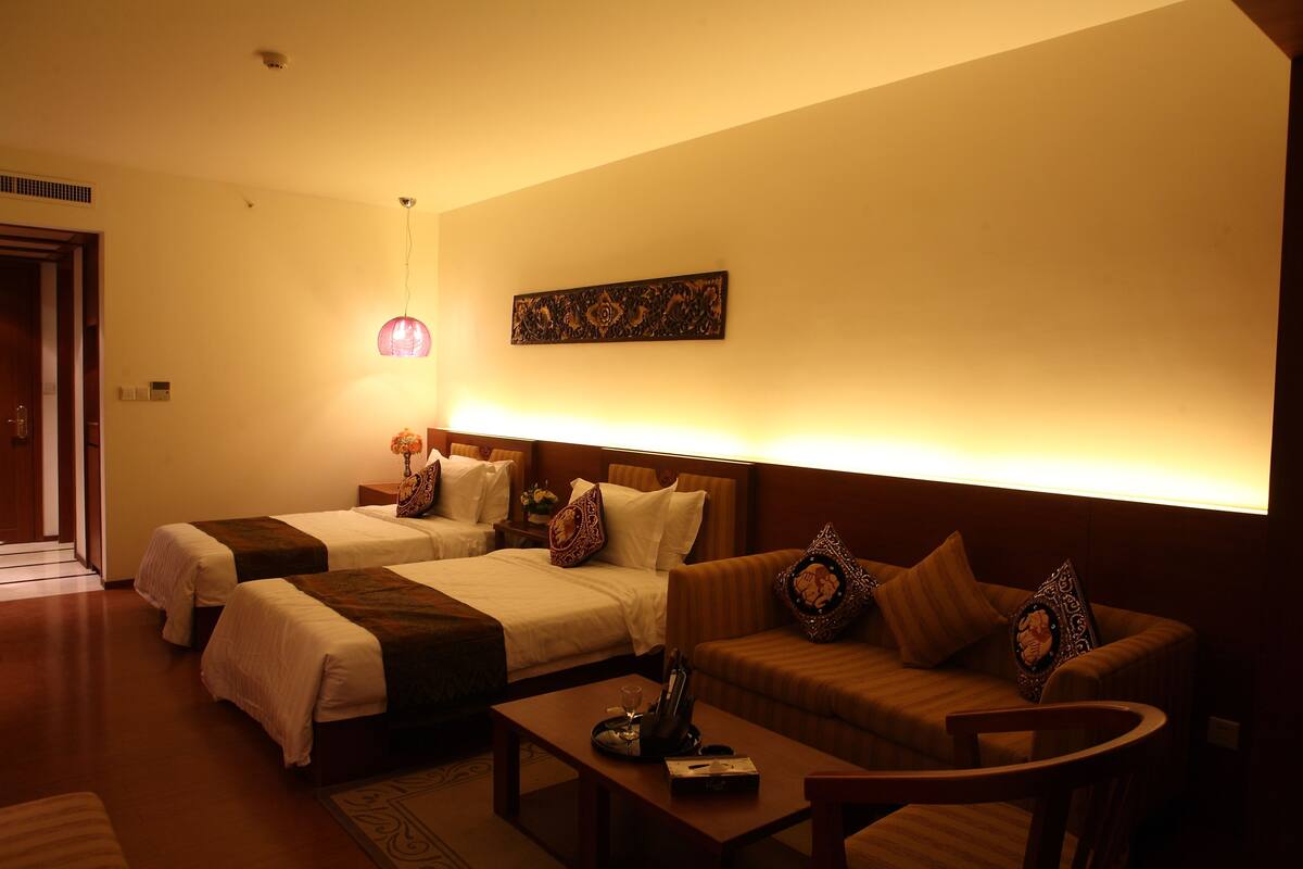 Quarto de hotel com duas camas, um sofá, uma mesa de centro e uma obra de arte na parede.