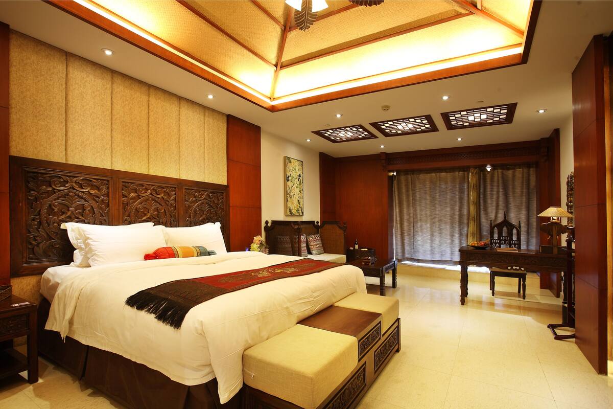 Quarto de hotel com uma cama grande, cabeceira de madeira, escrivaninha e uma cadeira.
