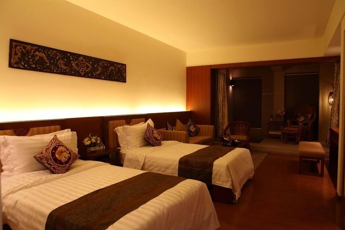 Quarto de hotel com duas camas, uma grande peça decorativa na parede e vista para a área do saguão.