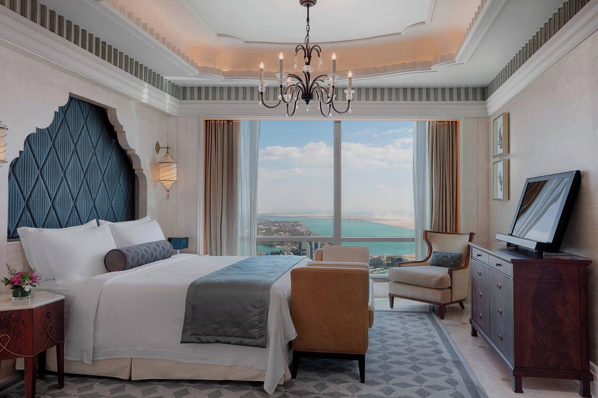 Quarto de hotel com uma cama grande, televisão, escrivaninha e vista para a cidade.