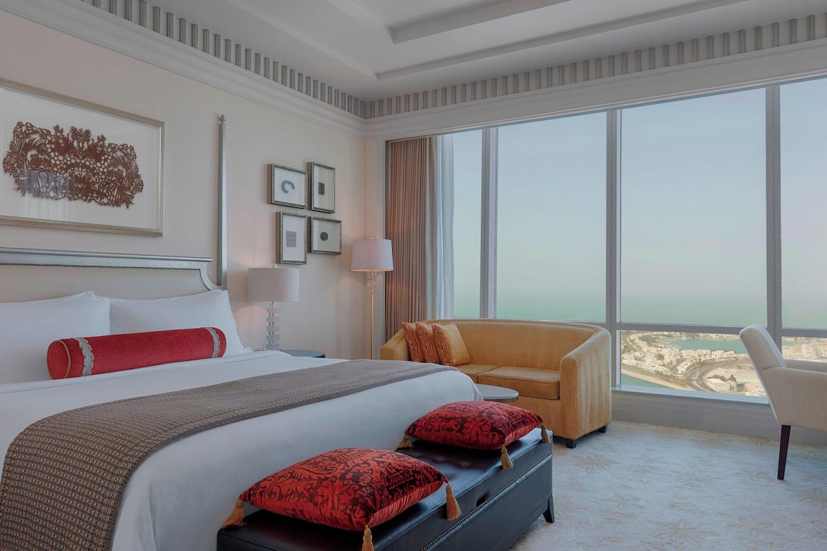 Quarto de hotel com uma cama grande, um sofá, uma cadeira e vista para a cidade.