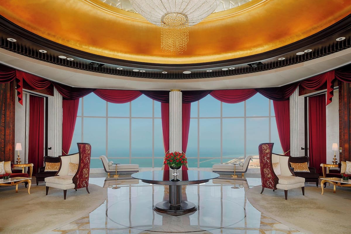Um lobby luxuoso com uma mesa redonda central, cadeiras elegantes e uma grande janela com vista.