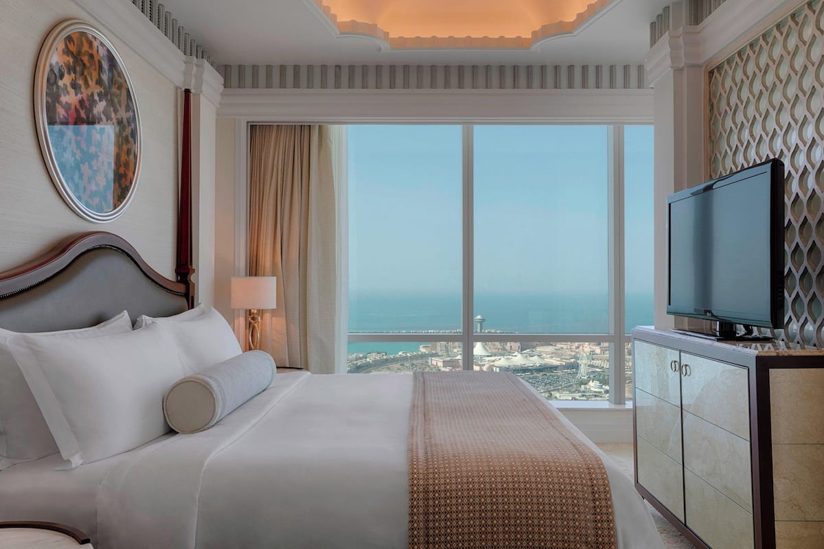 Quarto de hotel com uma cama grande, televisão e vista para a cidade e mar.