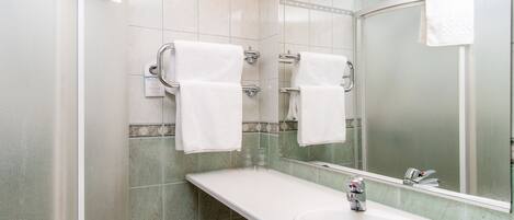Casa de banho com lavatório branco, espelho e duas barras de toalhas com toalhas brancas.