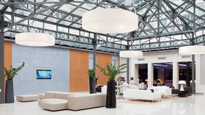 Um lobby amplo com móveis modernos, janelas grandes e teto alto com estrutura metálica.