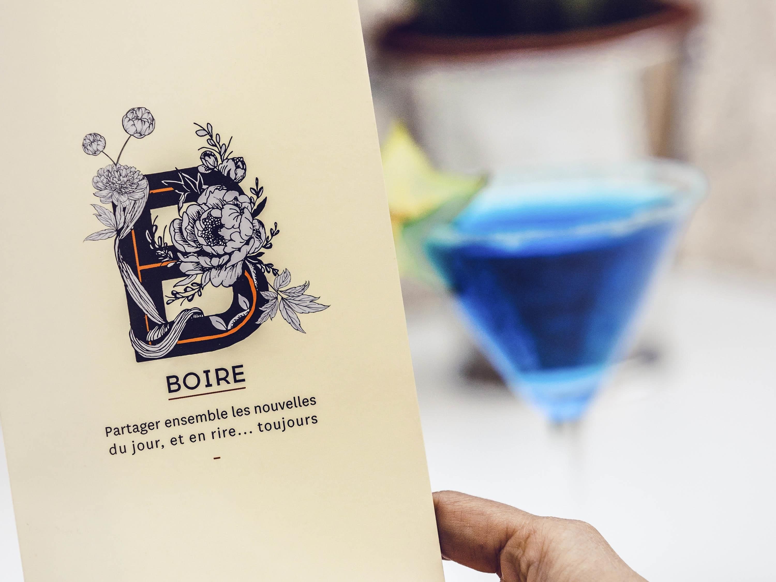 Mão segurando um cardápio com design floral e a palavra 'BOIRE' escrita.