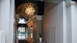 Um hall de hotel moderno com um longo corredor, um lustre grande, área de estar e um vaso de planta.