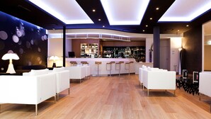 Uma área de bar moderna com banquetas brancas, um balcão e um espaço de estar com sofás brancos.
