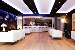 Uma área de bar moderna com banquetas brancas, um balcão e um espaço de estar com sofás brancos.